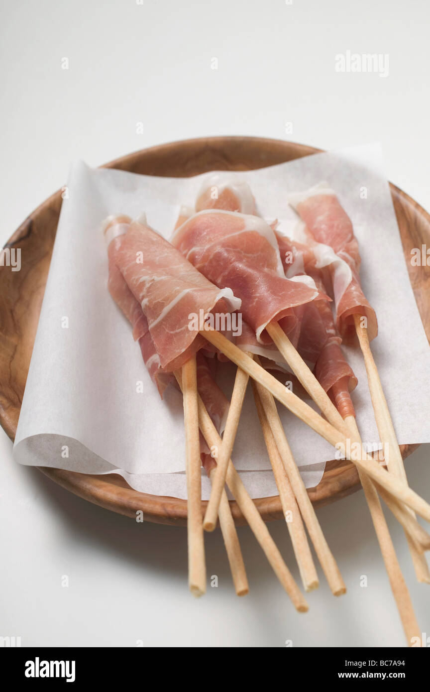 Grissini wrapped in raw ham on wooden plate Stock Photo - Alamy