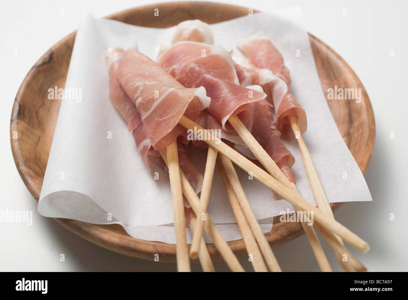 Grissini wrapped in raw ham on wooden plate Stock Photo - Alamy