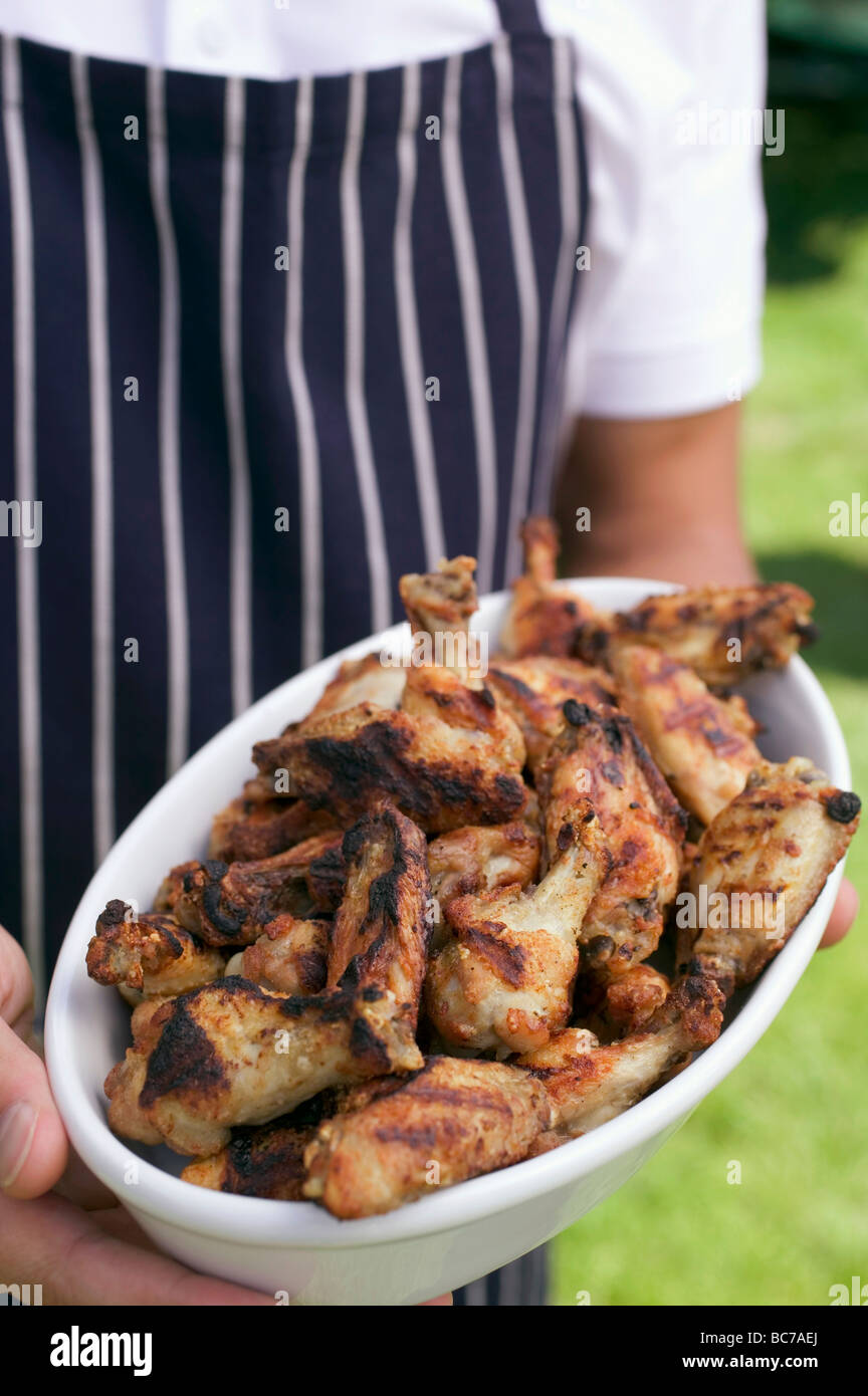 Man in apron holding grilled chicken wings Stock Photo - Alamy
