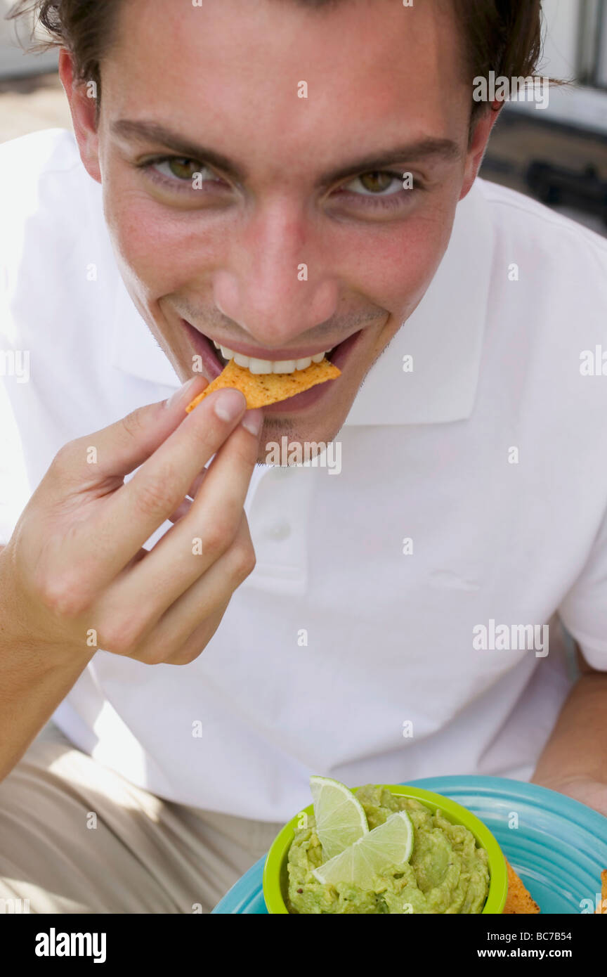 Young man eating tortilla chips with guacamole Stock Photo - Alamy