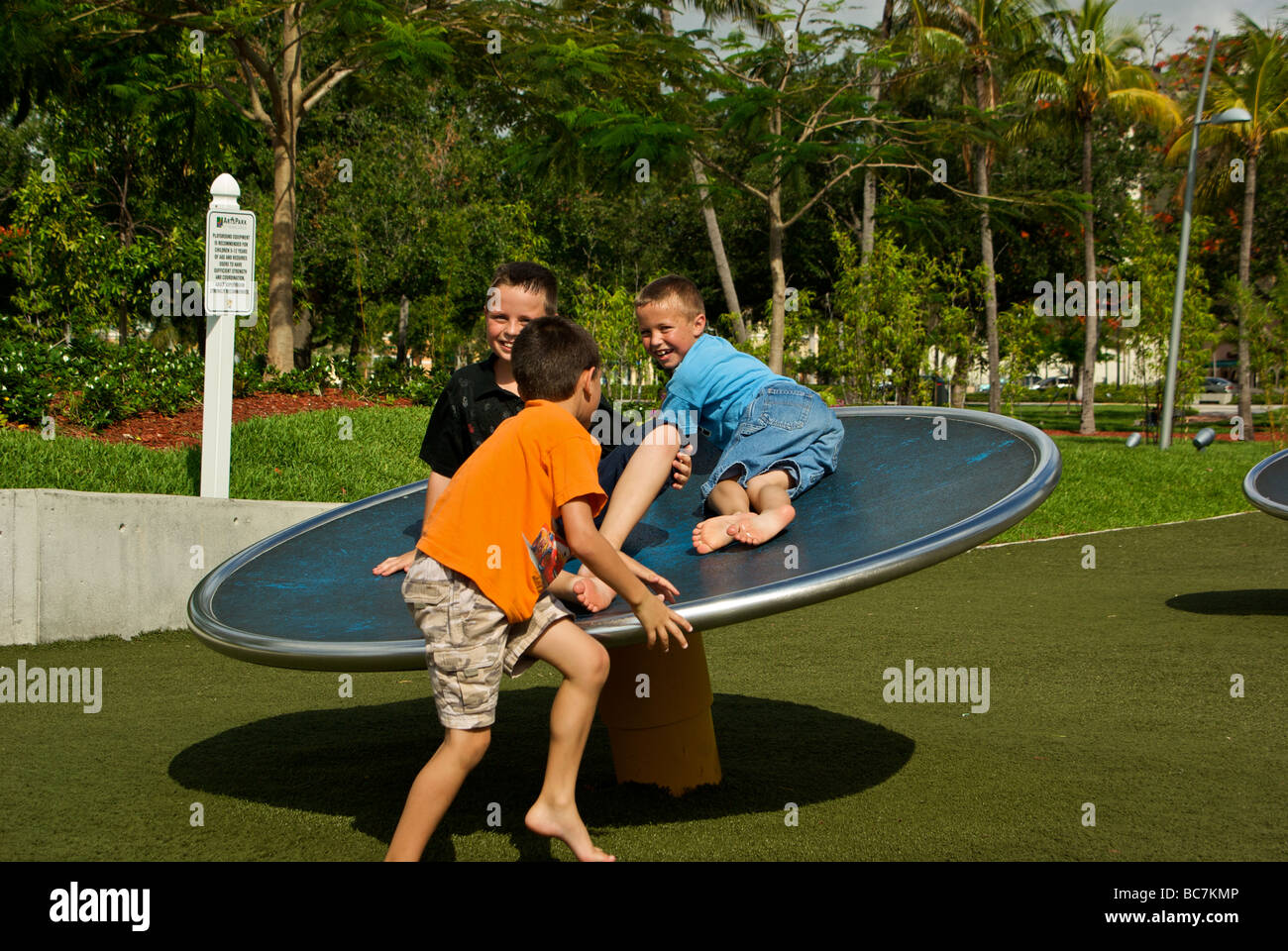 Three young barefoot boys laughing spinning on big rotating disk at ...