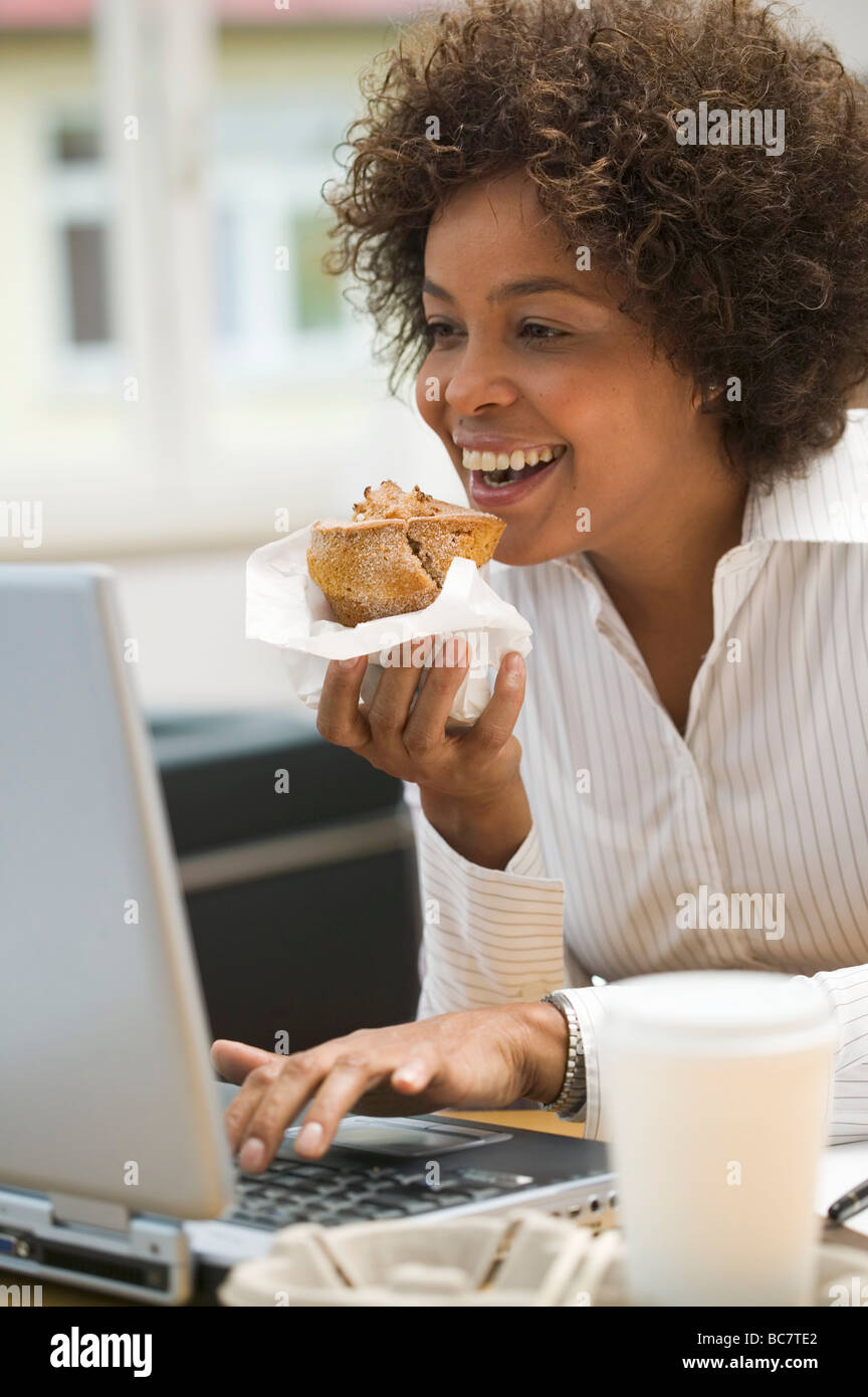 Woman eating muffin while working on computer Stock Photo - Alamy