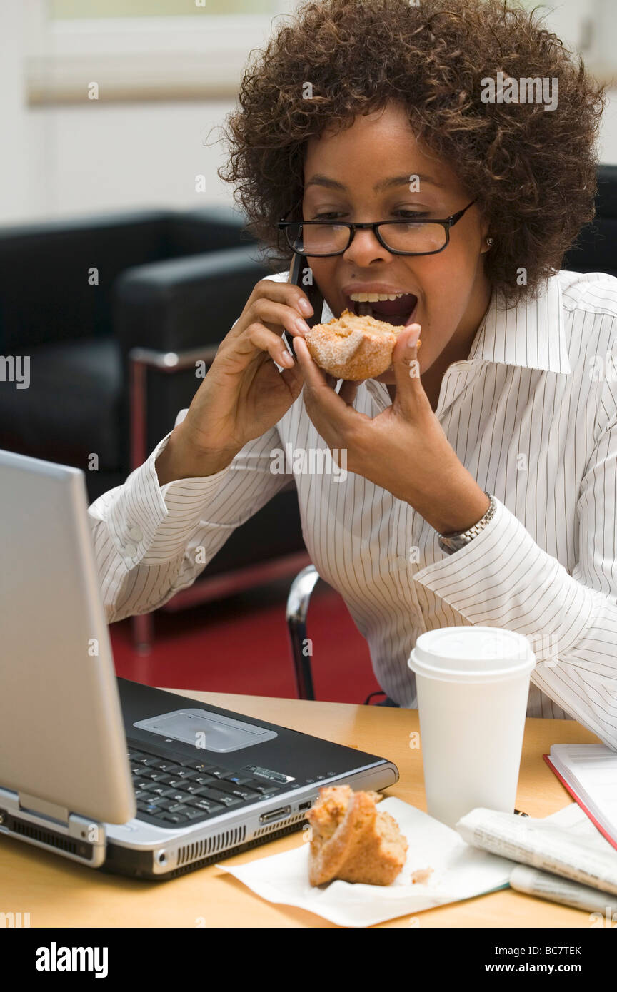Woman eating muffin while working on computer Stock Photo - Alamy