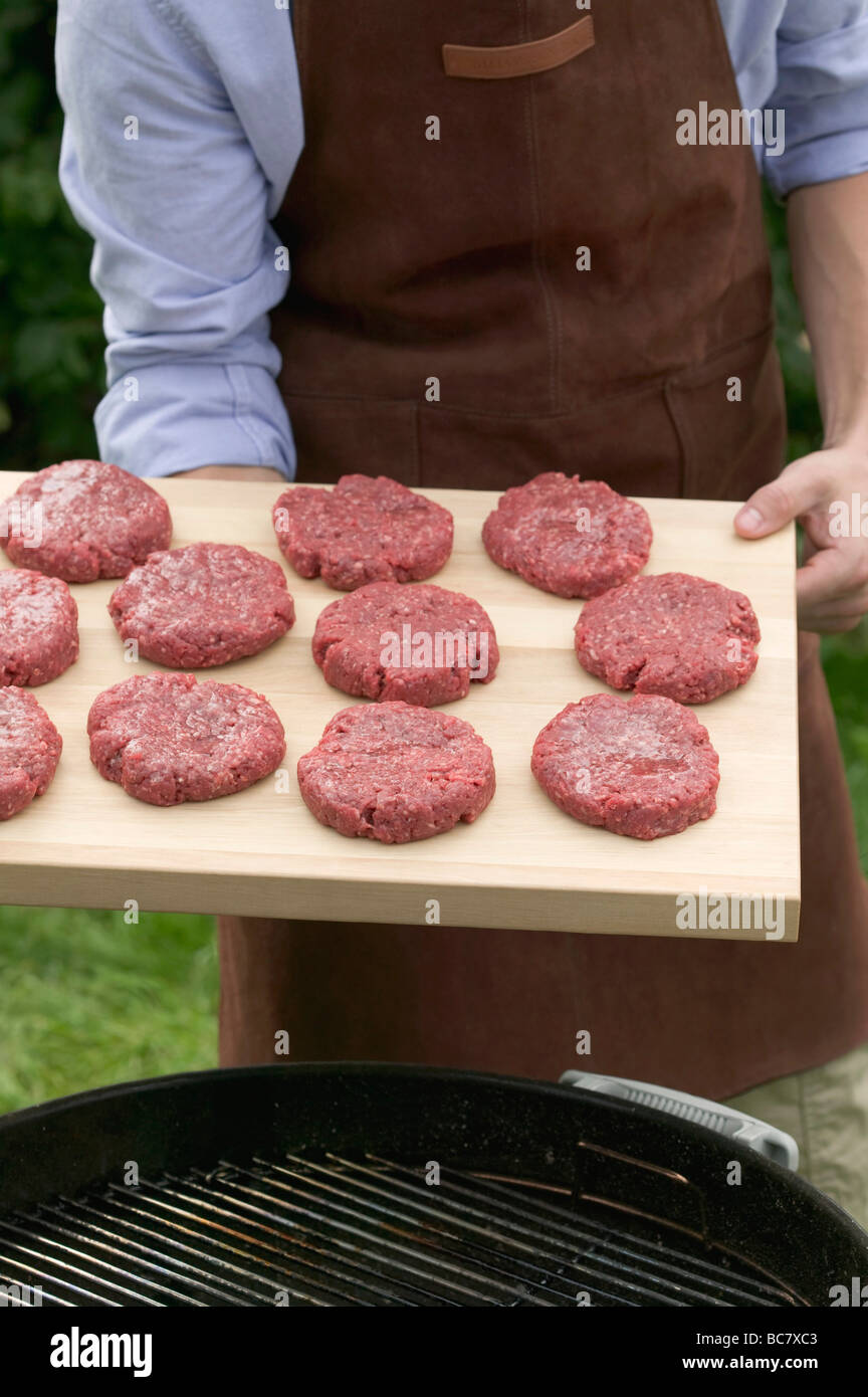 Man holding raw burgers on chopping board over barbecue Stock Photo - Alamy