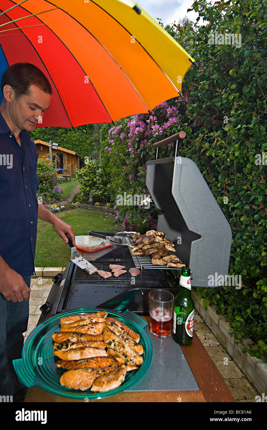 Humourous vertical wide angle of a man standing cooking on a barbeque ...