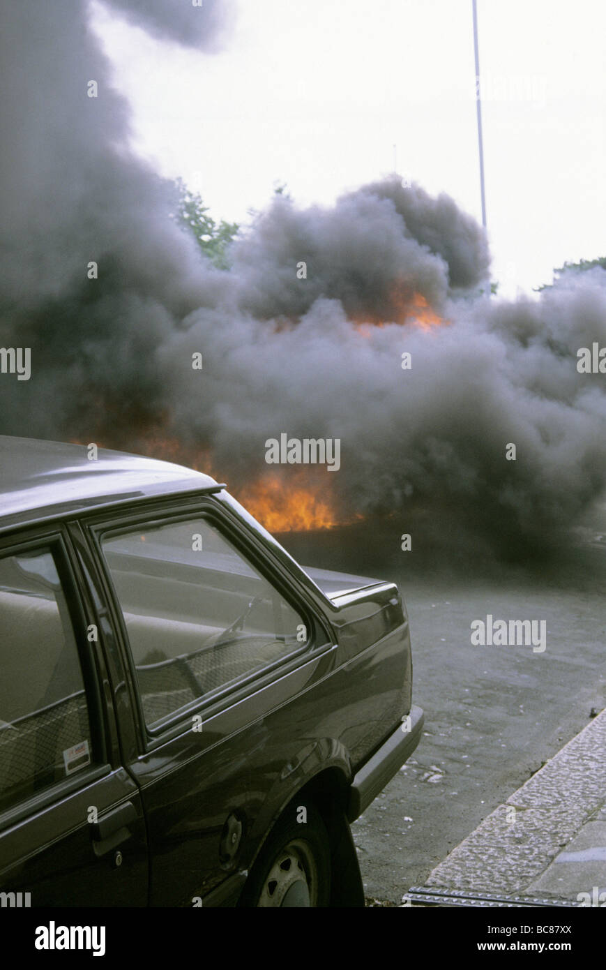 Car ablaze on fire in middle of street road billowing thick black smoke ...