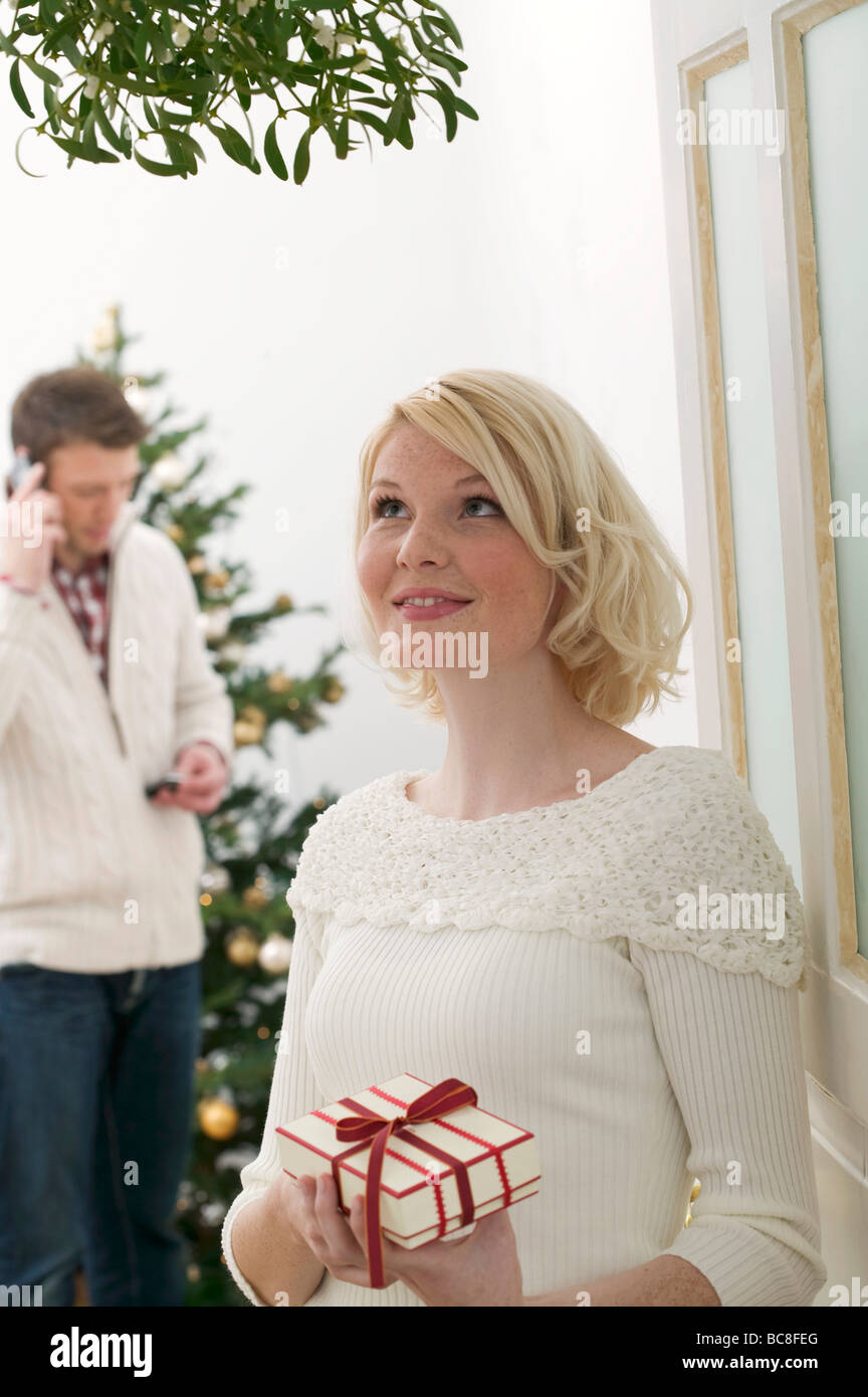 Woman with gift under mistletoe, man in background Stock Photo - Alamy