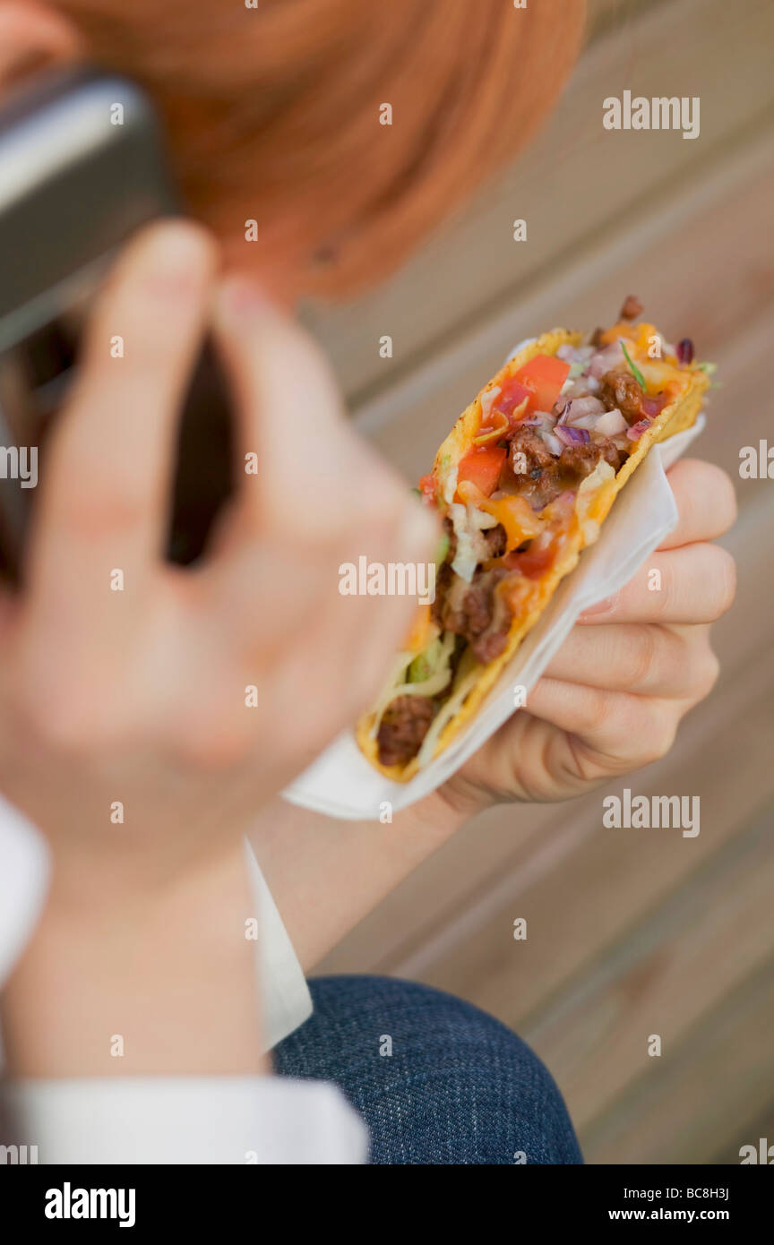 Woman on the phone with a taco in her hand Stock Photo - Alamy
