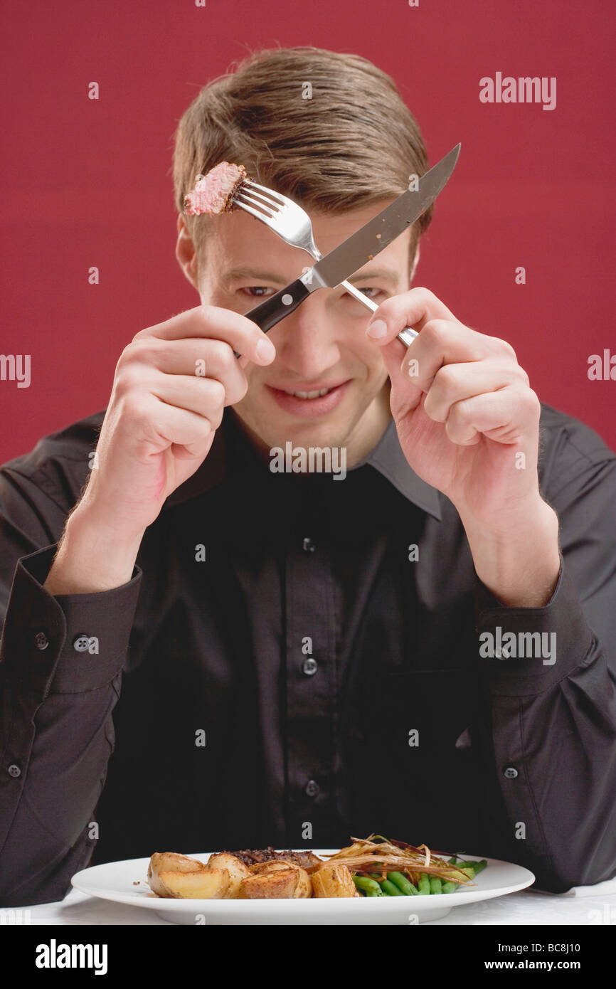 Man crossing knife and fork in front of his face Stock Photo - Alamy