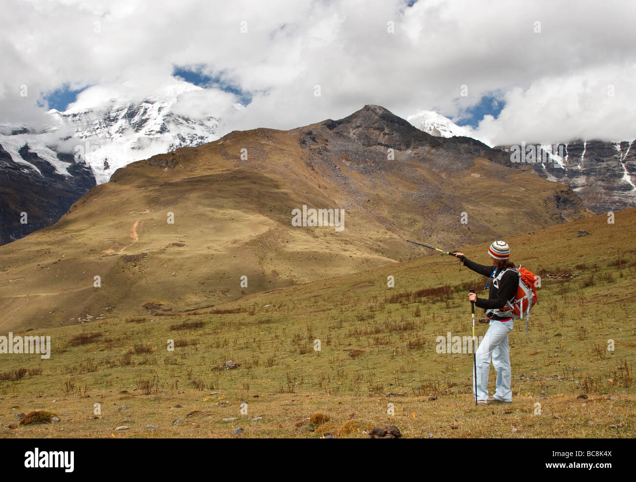 A woman points over t Mt. Jomolhari while trekking across a hillside in ...