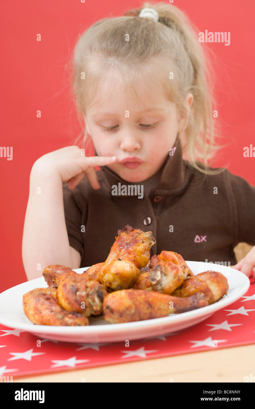 Little girl looking at plate of chicken drumsticks Stock Photo - Alamy