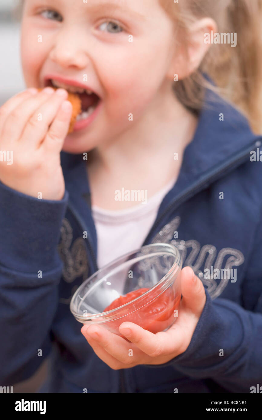 Little girl eating chicken nugget with ketchup Stock Photo - Alamy