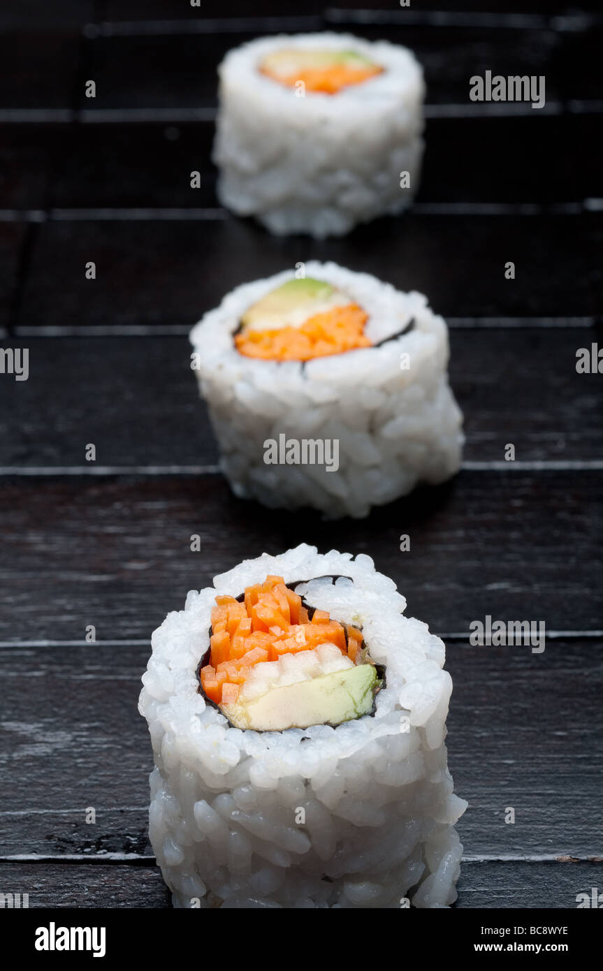 shallow focus vertical macro of 3 rolls of sushi on black wood Stock ...