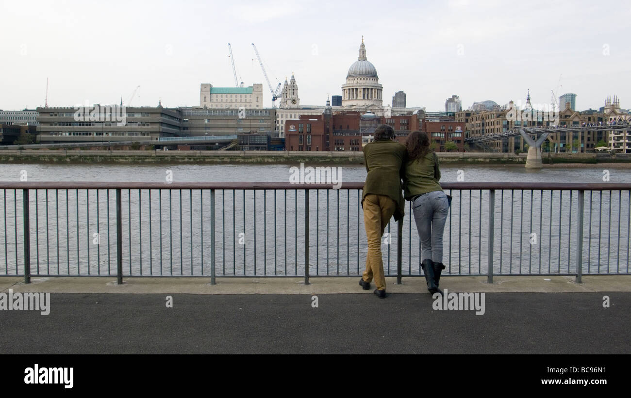Couple leaning on a railing over a river with the city skyline behind ...