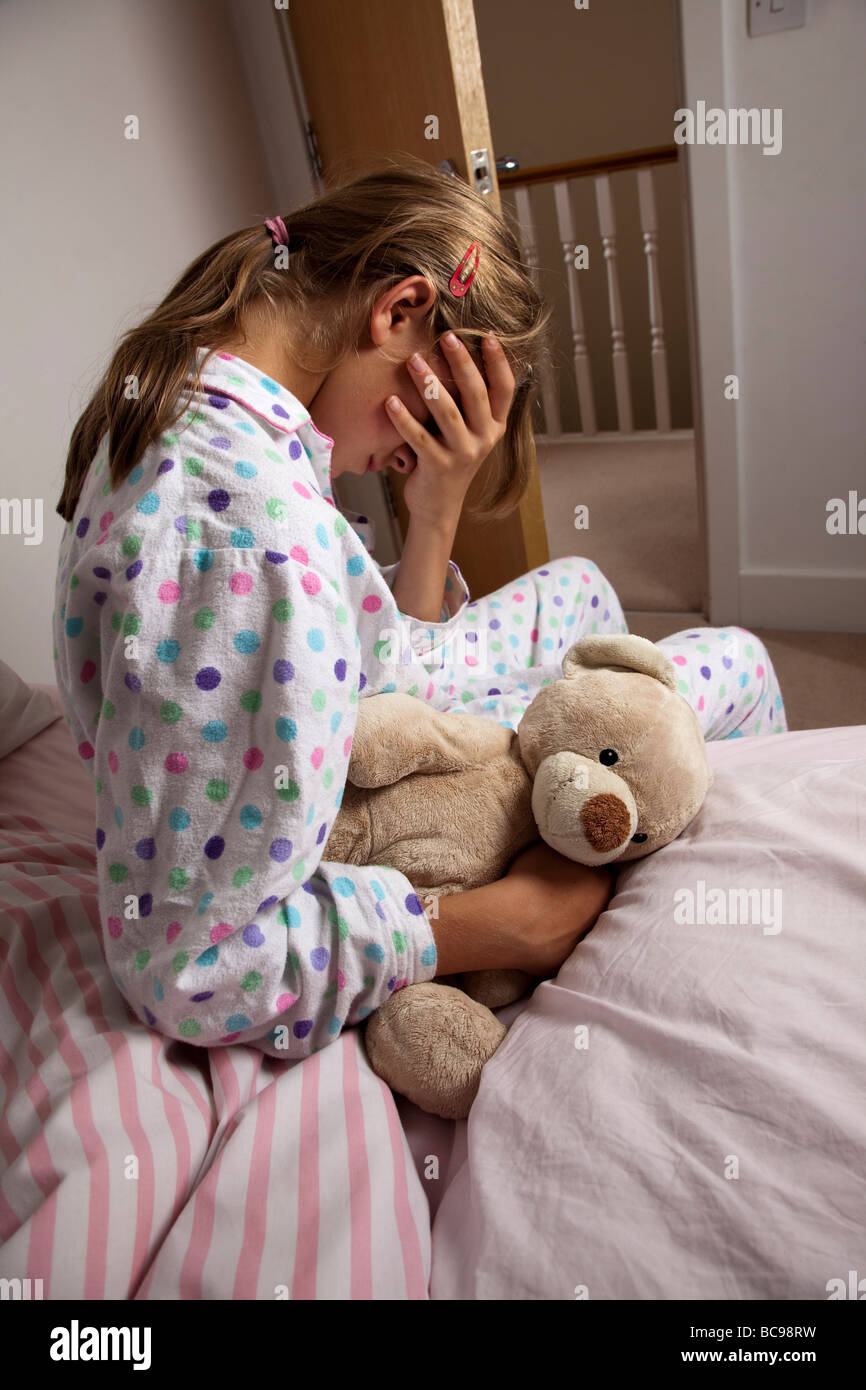 Young pony tailed girl wearing pyjamas sitting on her bed head down ...