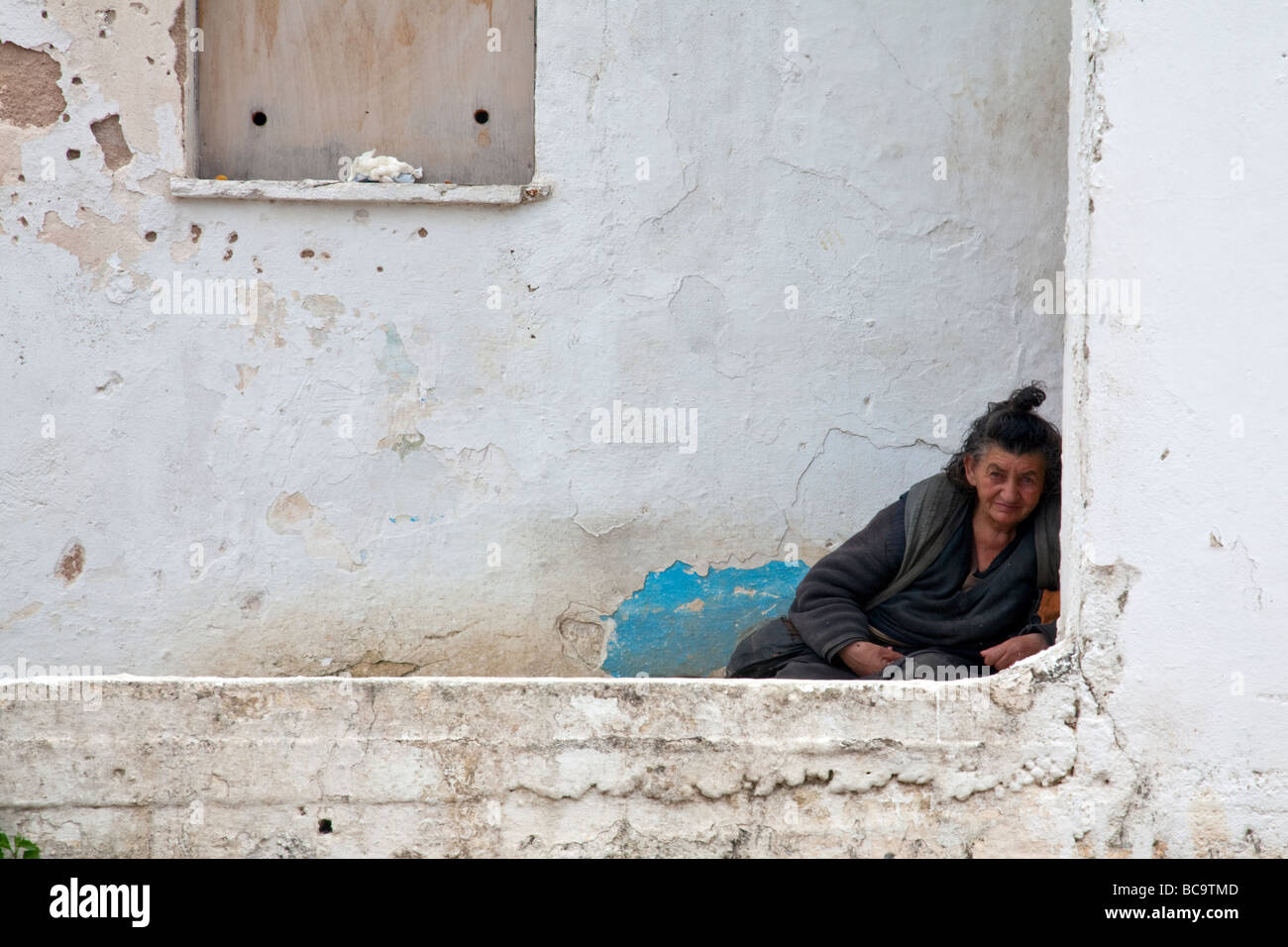 Old tramp lady trying keep warm against a cold damp wall in Argostoli ...