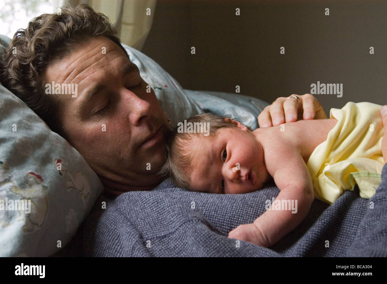 A father takes a nap with his newborn daughter who slowly awakens Stock ...