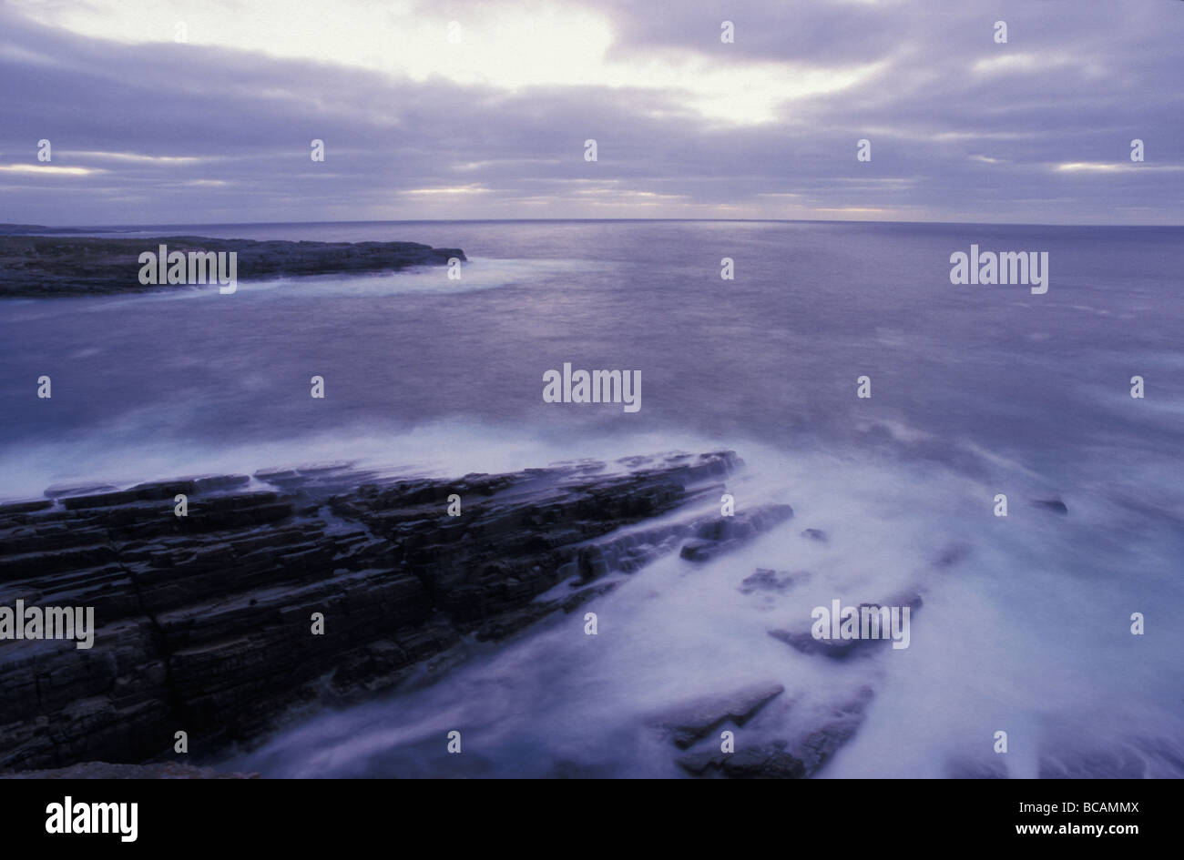 Huge waves break against a jagged rock cliff face after sunset Stock ...