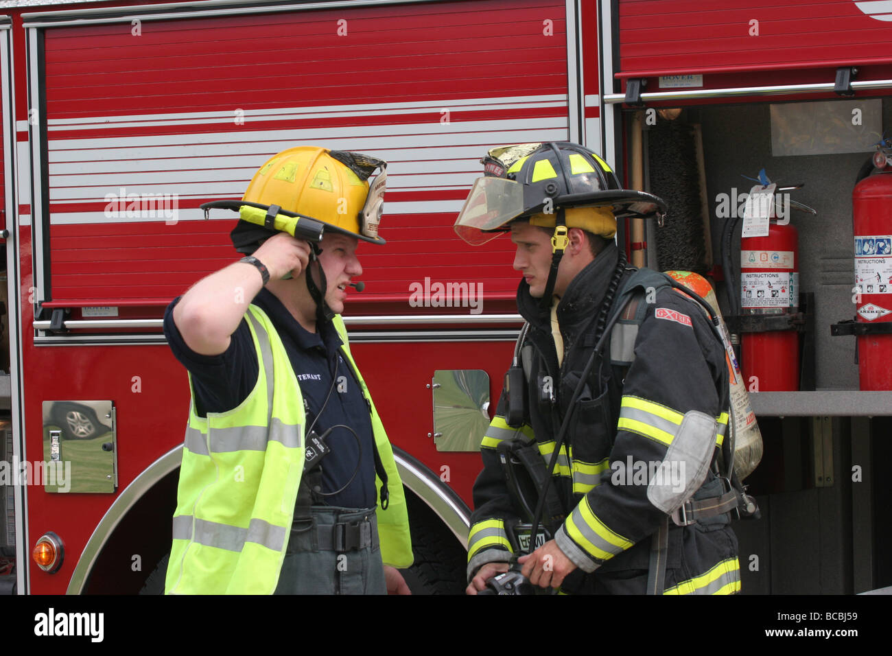 Two firefighters talking in front of the pumper engine at a fire scene ...