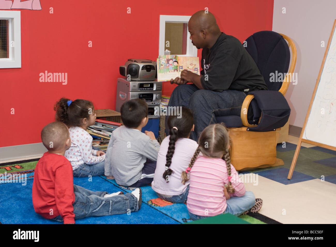African American male preschool teacher reading a book to his students ...