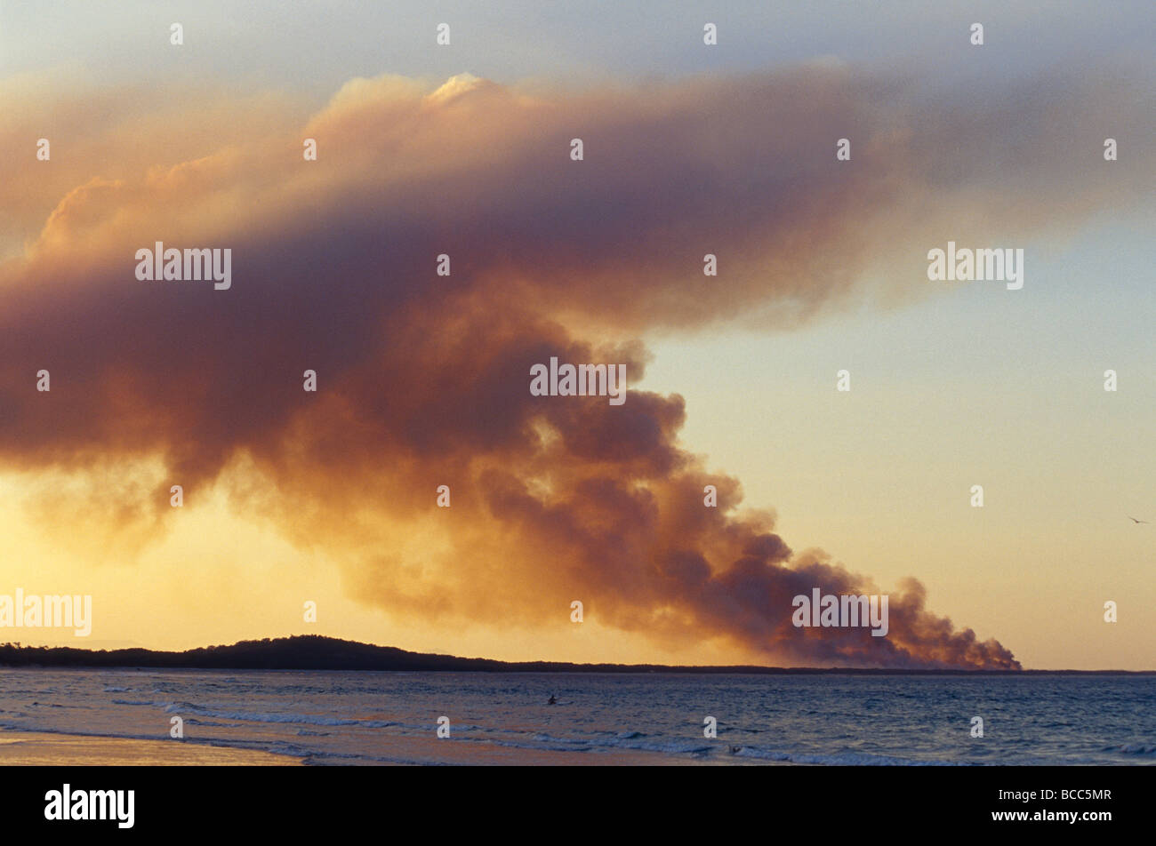 Smoke from a wildfire billows across a calm Bay at sunset Stock Photo ...