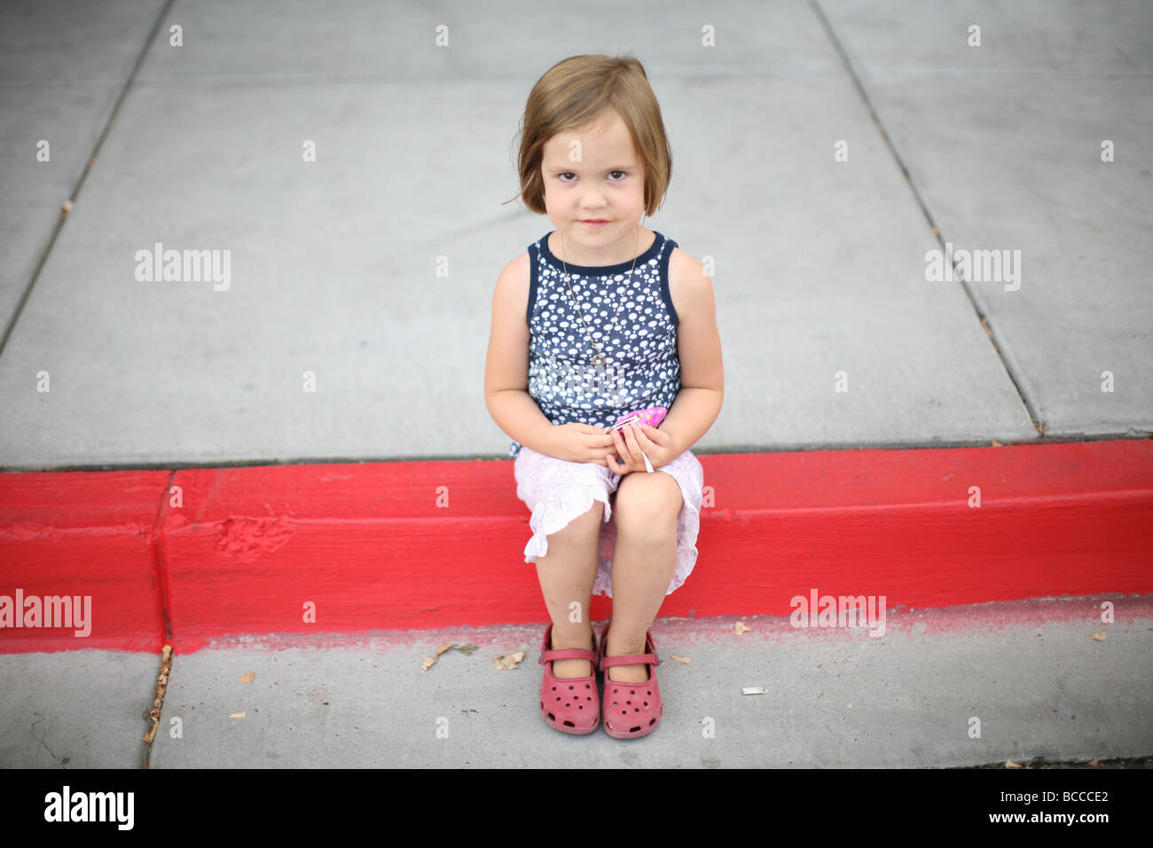 Portrait of young girl sitting on curb Stock Photo - Alamy