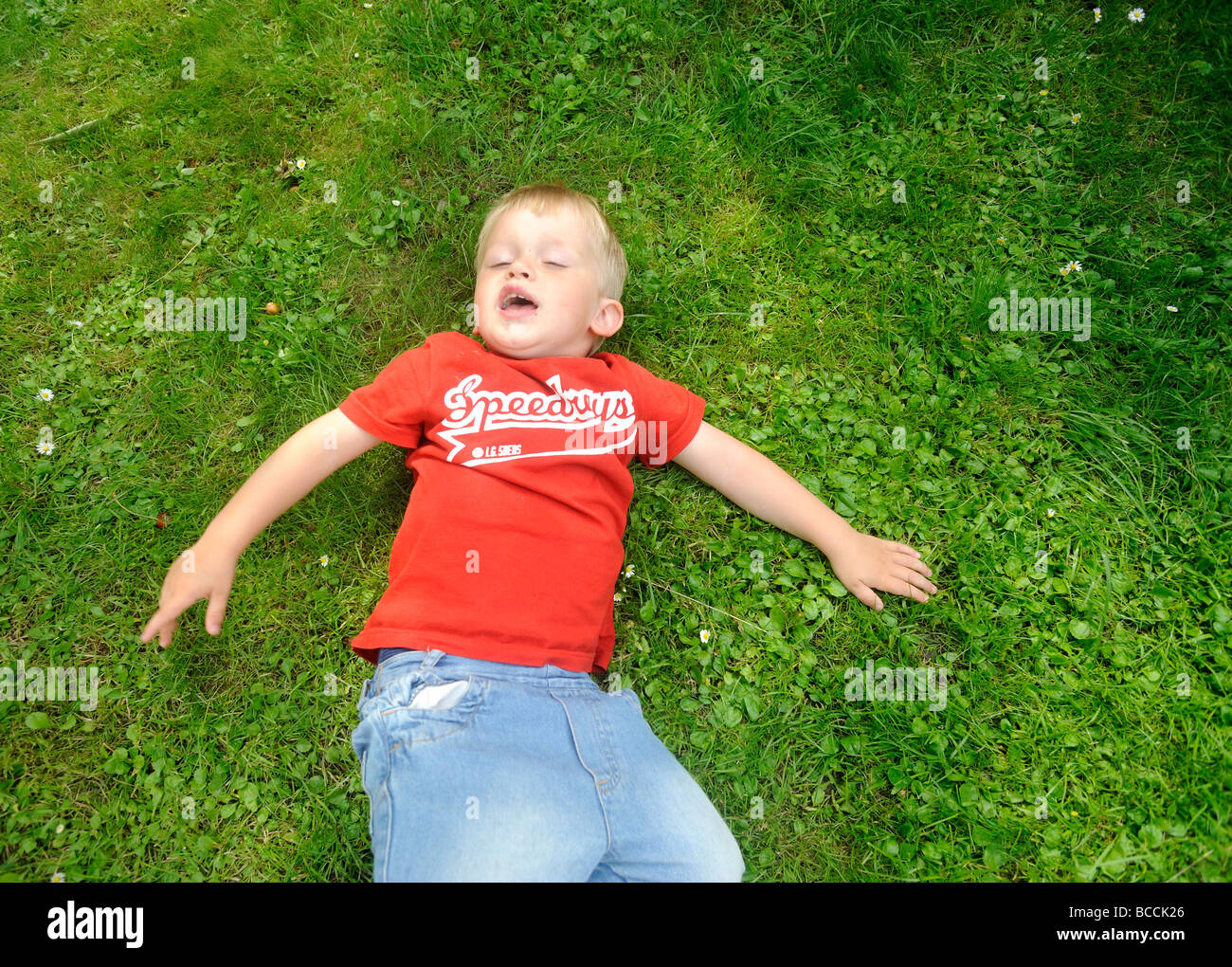 young child smiling blond boy lying on a green lawn playing with mother ...