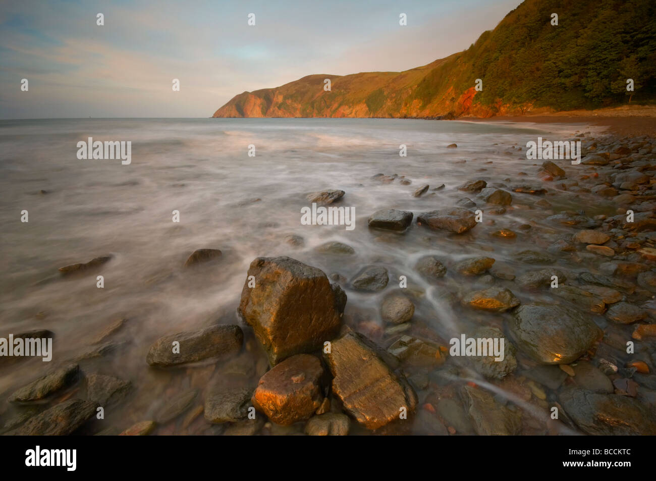 Low evening sunlight illuminates rocks on the shore at Foreland Point ...