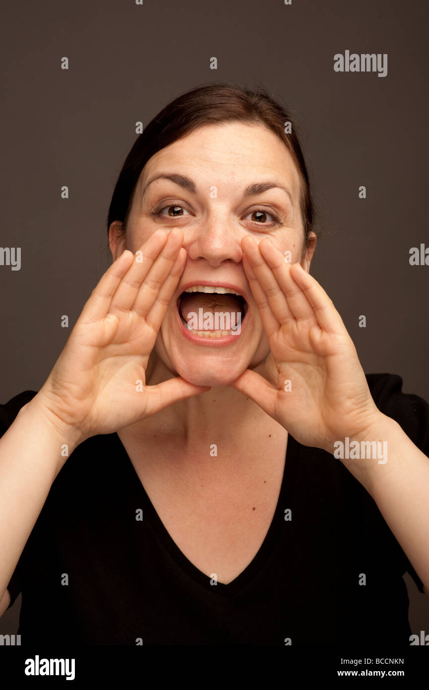 A Brown haired woman cupping her hands to her mouth shouting yelling ...