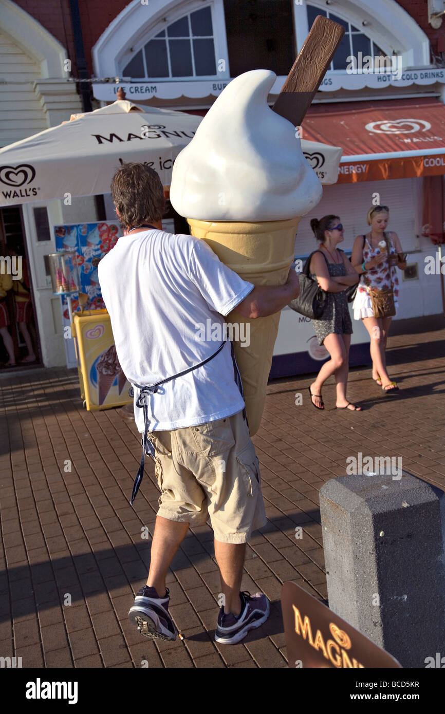 a man carrying a model of an ice cream on brighton beach in england ...