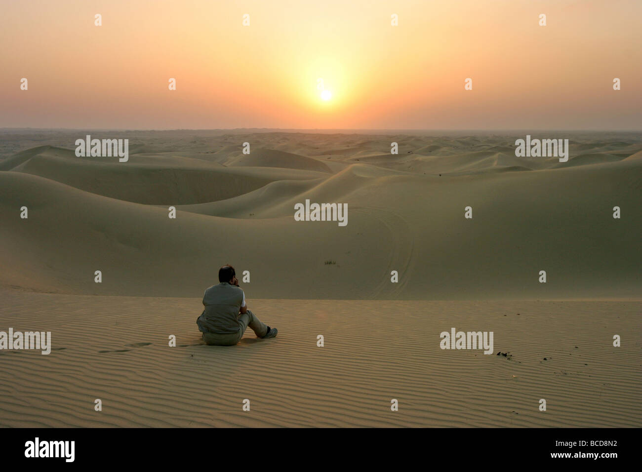 A man sitting watching the sunset in the arabian desert, Abu Dhabi, UAE ...