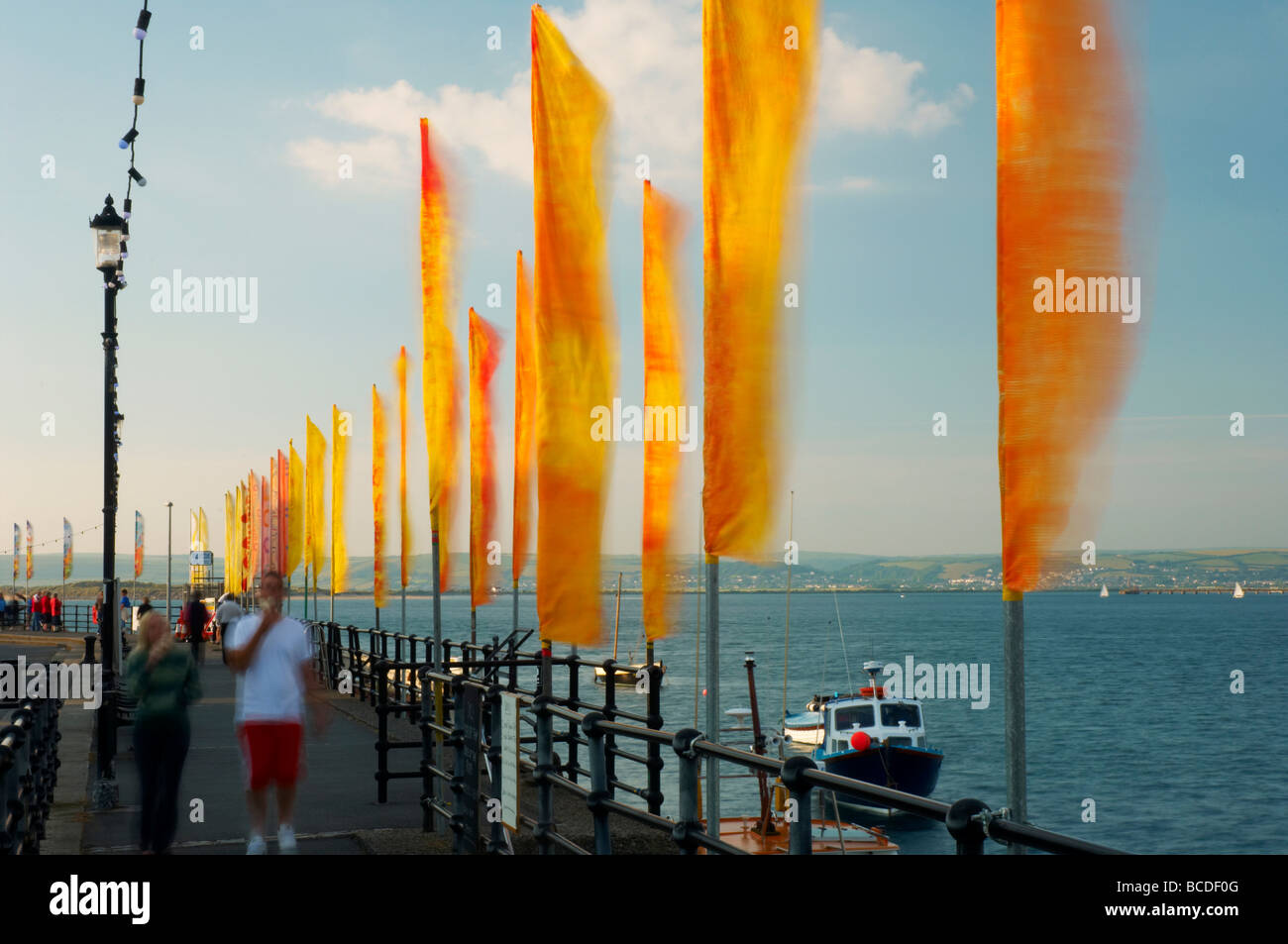 Crowds of people walking past brightly coloured flags flapping in the ...