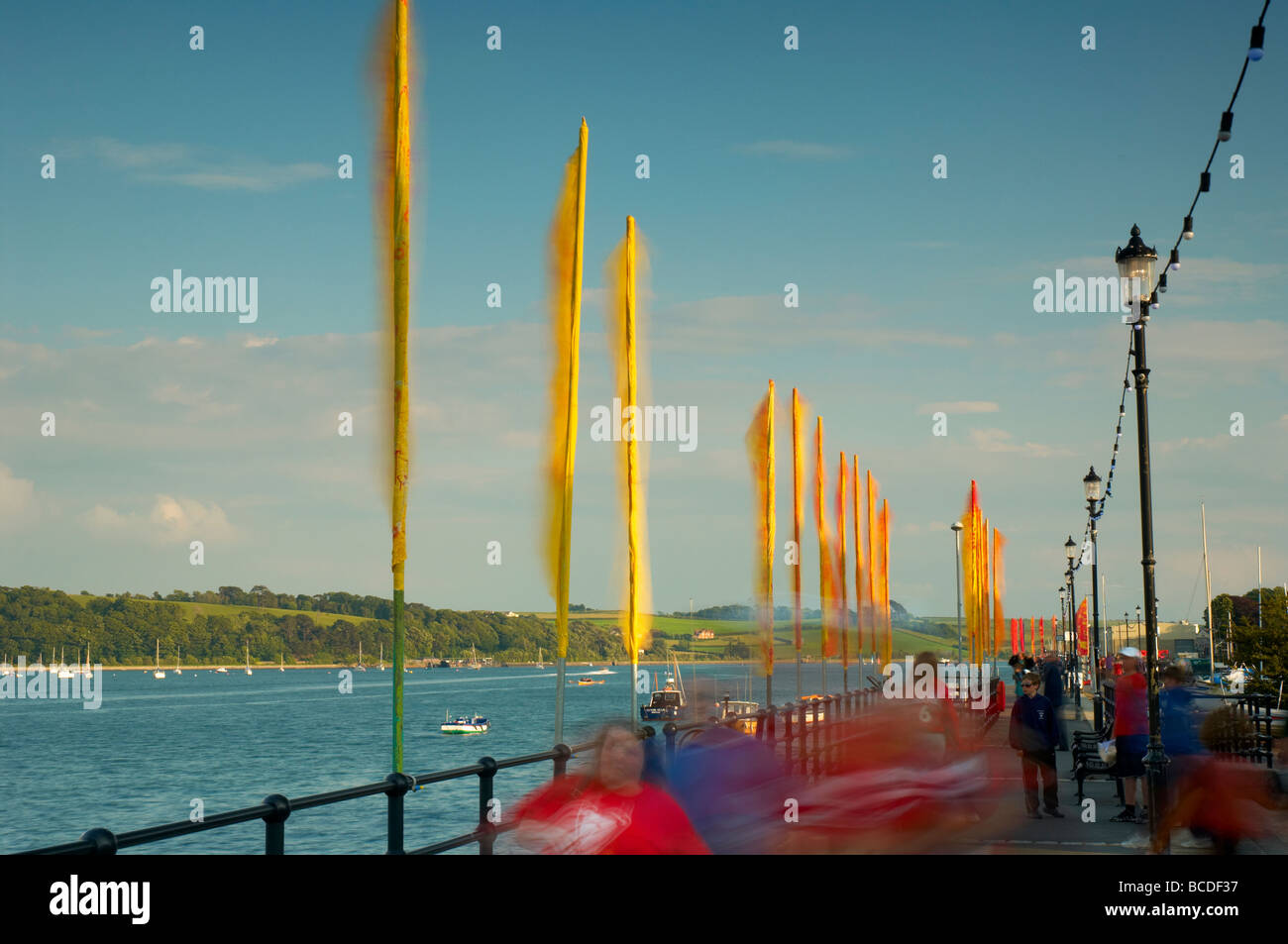 Crowds of people walking past brightly coloured flags flapping in the ...