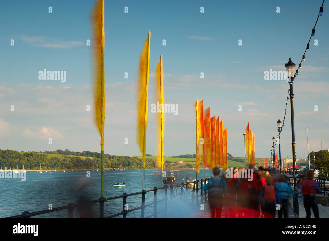 Crowds of people walking past brightly coloured flags flapping in the ...