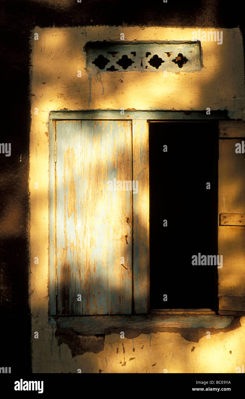 Sunset shadows fall on the painted shutters of a village hut window ...