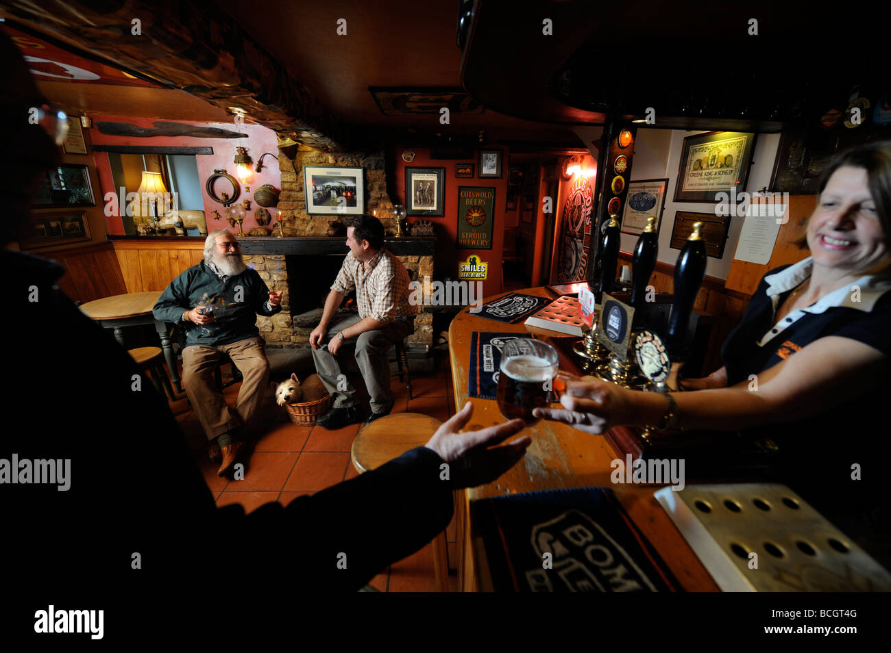TWO MEN SIT BY AN OPEN FIRE IN A TRADITIONAL PUB AS THE LANDLADY HANDS ...