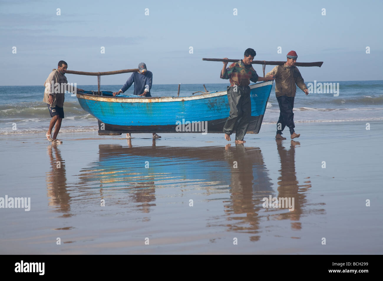 Blue Fishing Boat being carried by four men on the beach at Taghazoute ...
