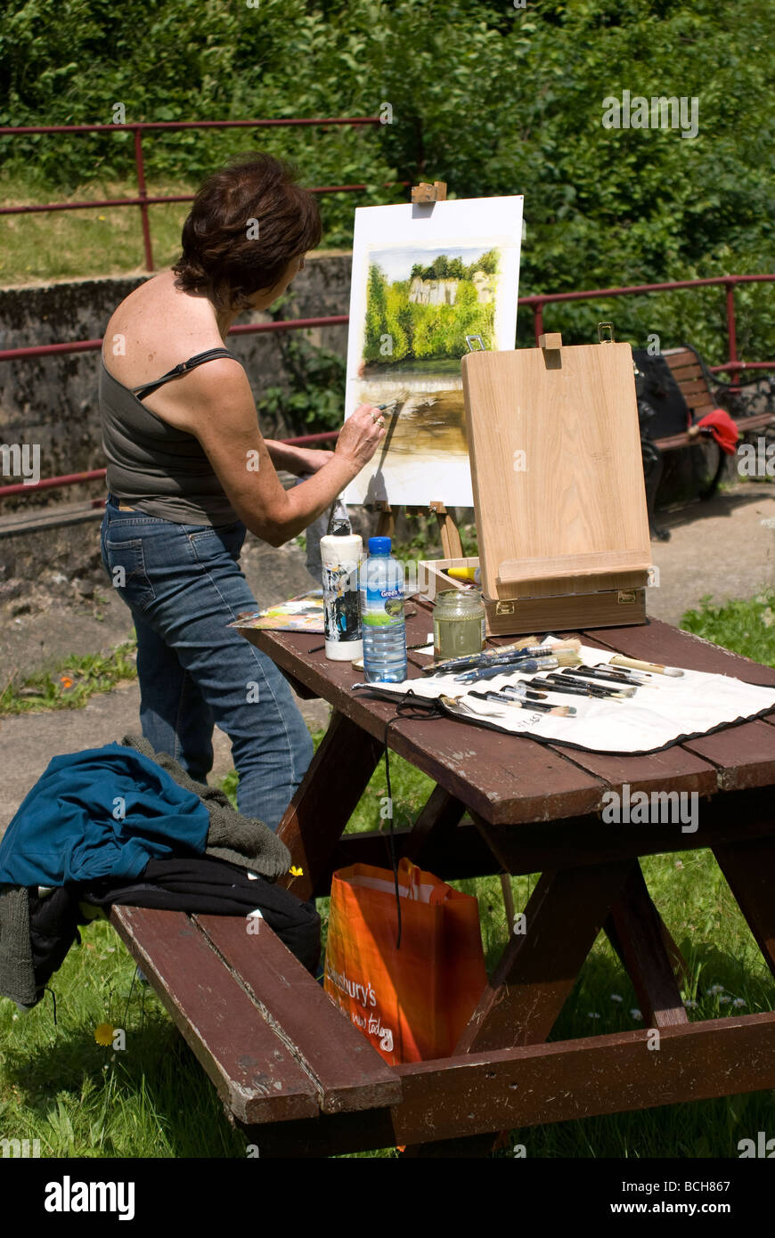 Female artist paints a picture at her easel in the English countryside ...
