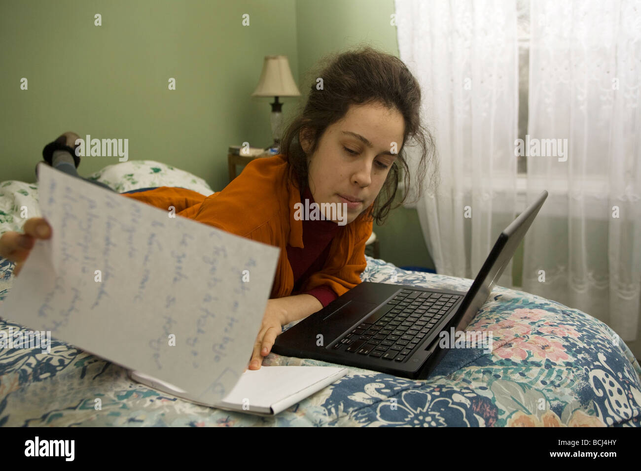 Female college student works on a wireless internet network on her bed ...