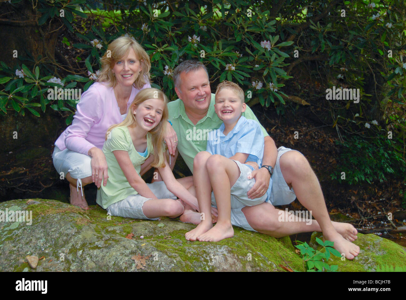family of four posing on rock for an outdoor portrait smiling and ...