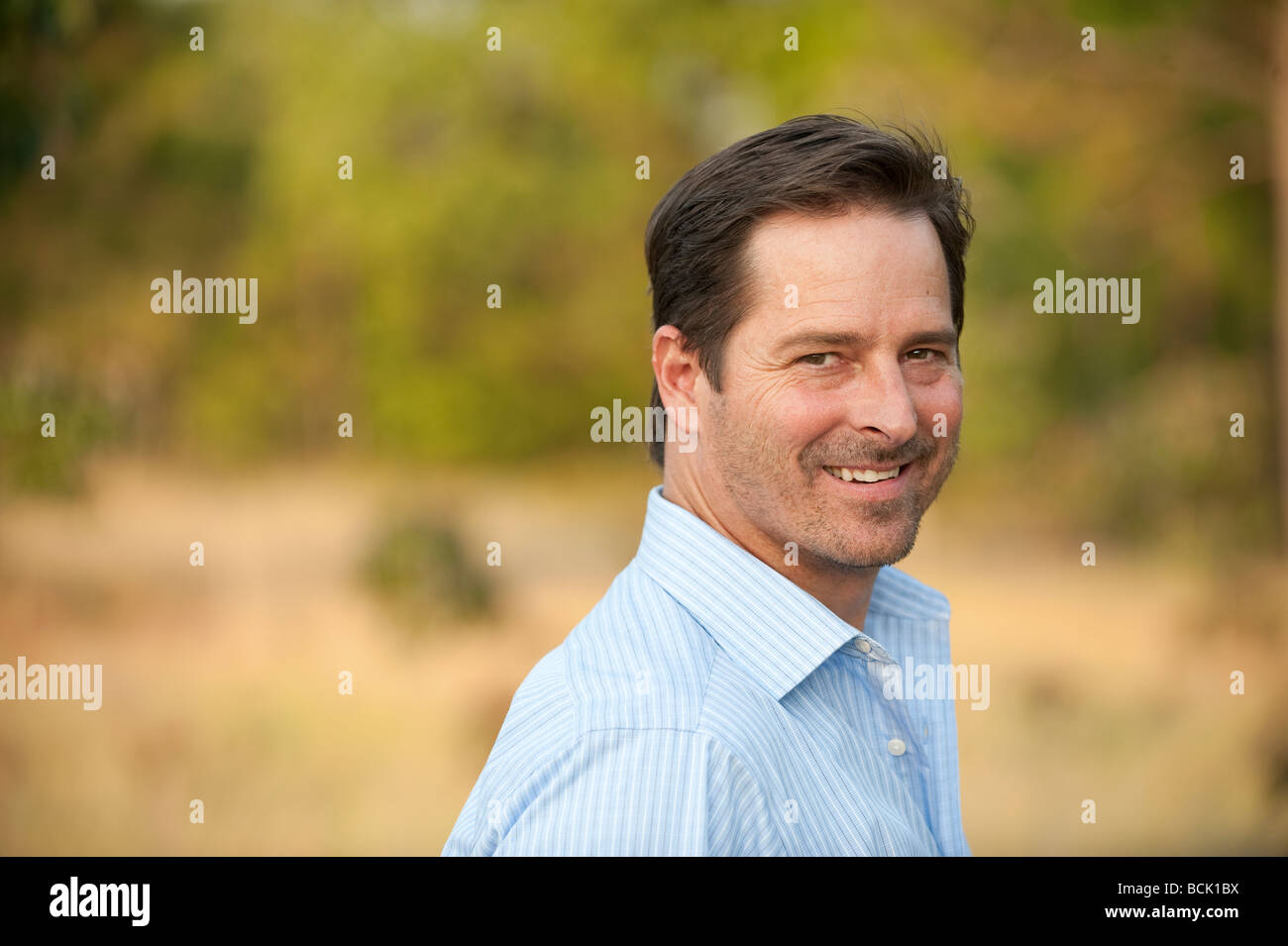 Man in a blue button down shirt looking back smiling Stock Photo - Alamy