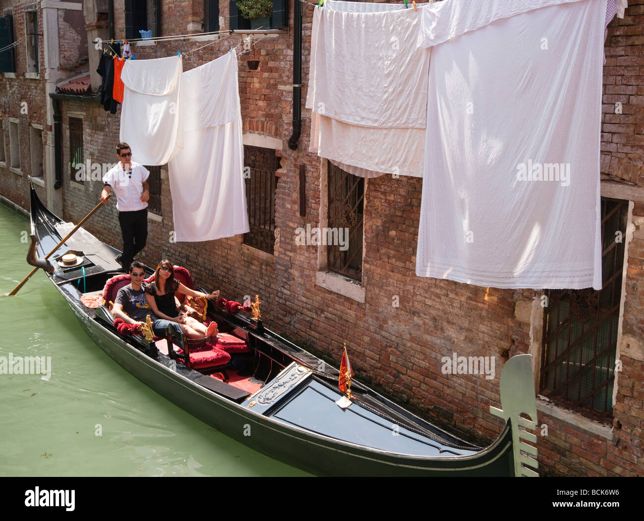 Venice - gondoliers and gondolas sailing below the washing - three ...