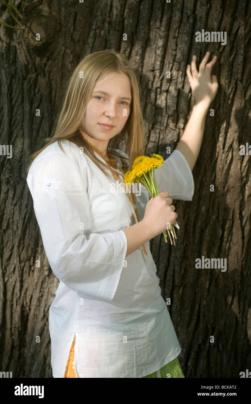 Girl standing by tree and holding flowers in hand Stock Photo - Alamy