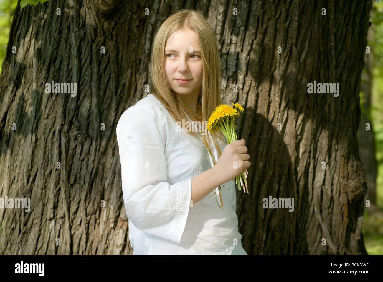 Girl standing by tree and holding flowers in hand Stock Photo - Alamy