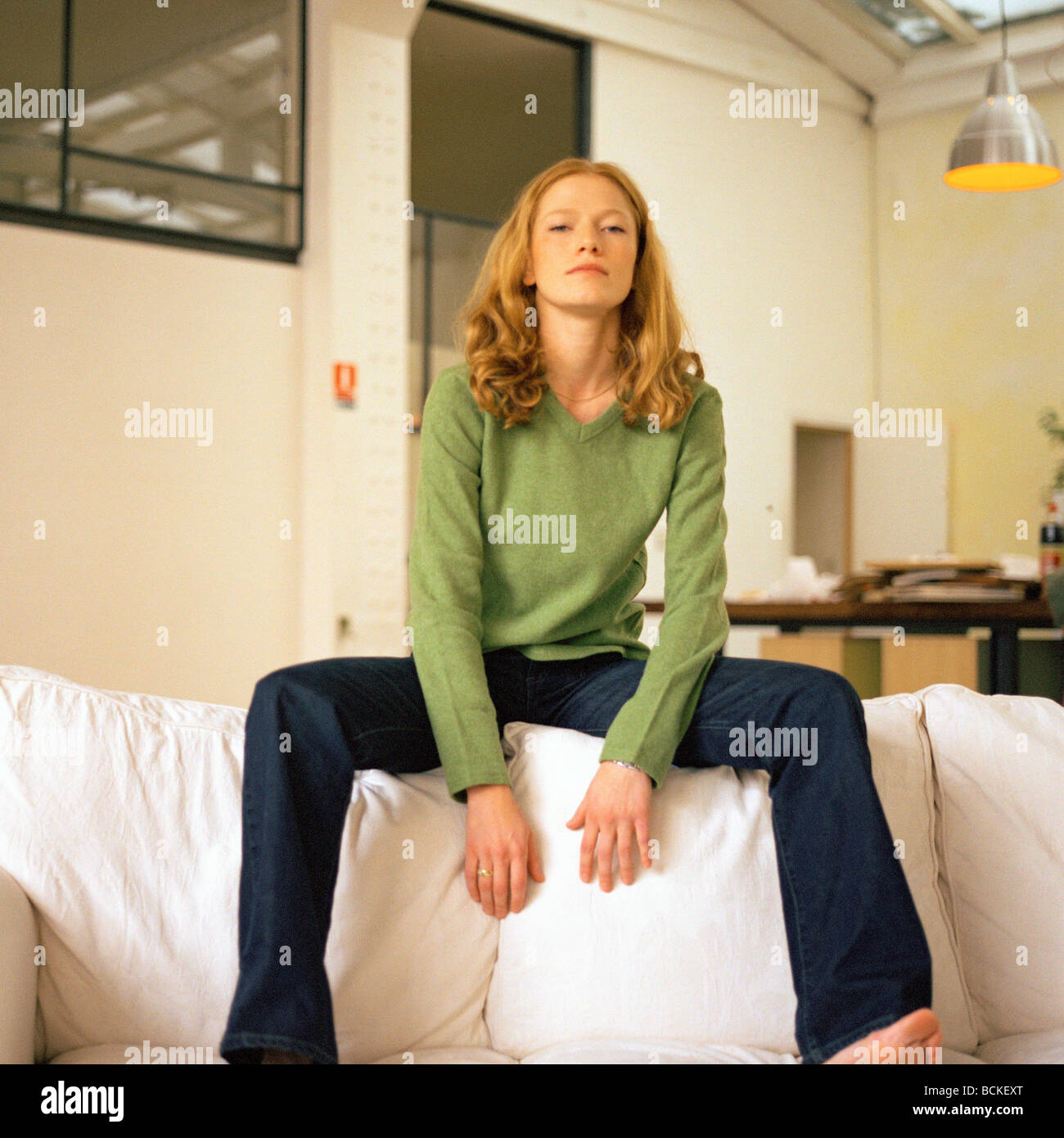 Young woman sitting on back of sofa Stock Photo - Alamy
