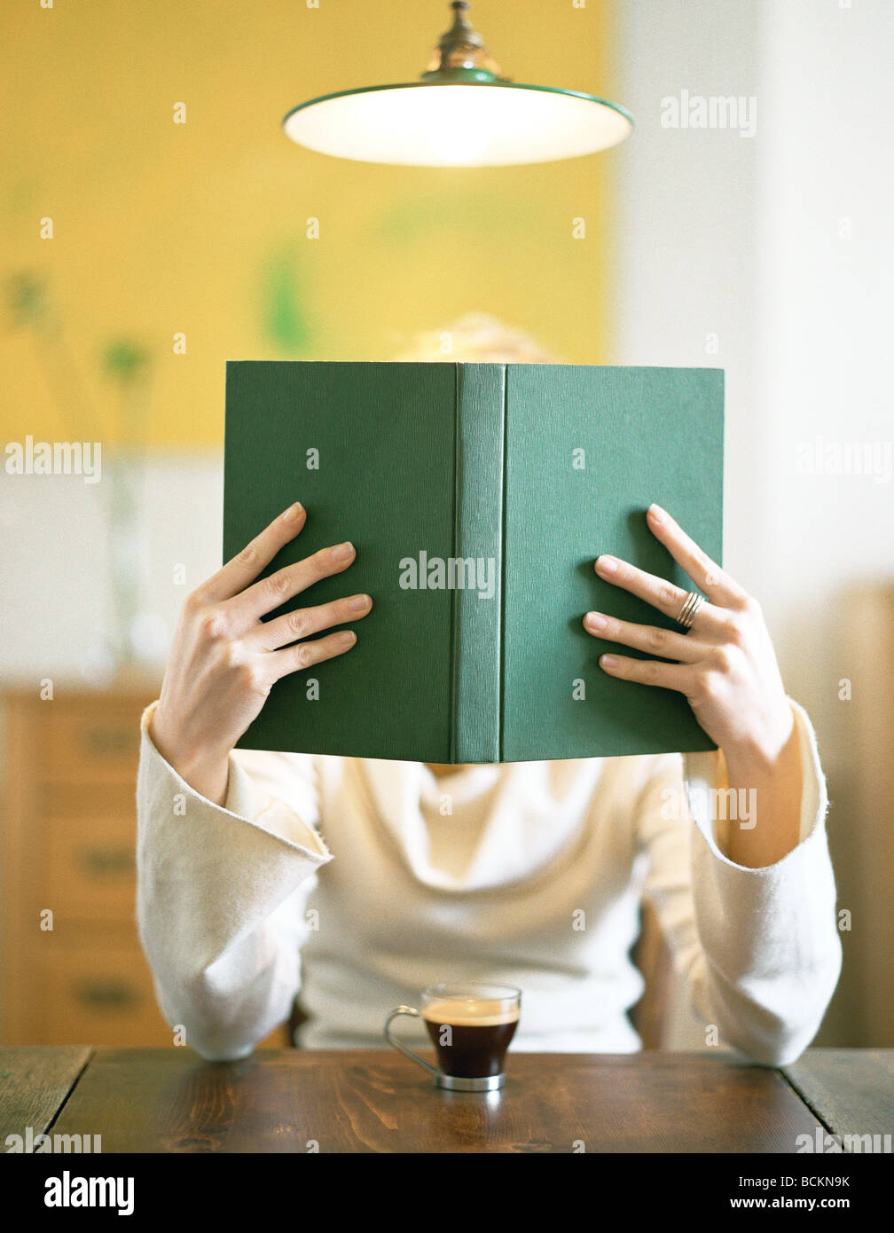 Woman sitting at table reading book Stock Photo - Alamy