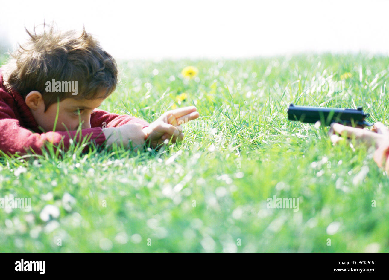 Child lying on grass pointing fingers like gun across from second ...