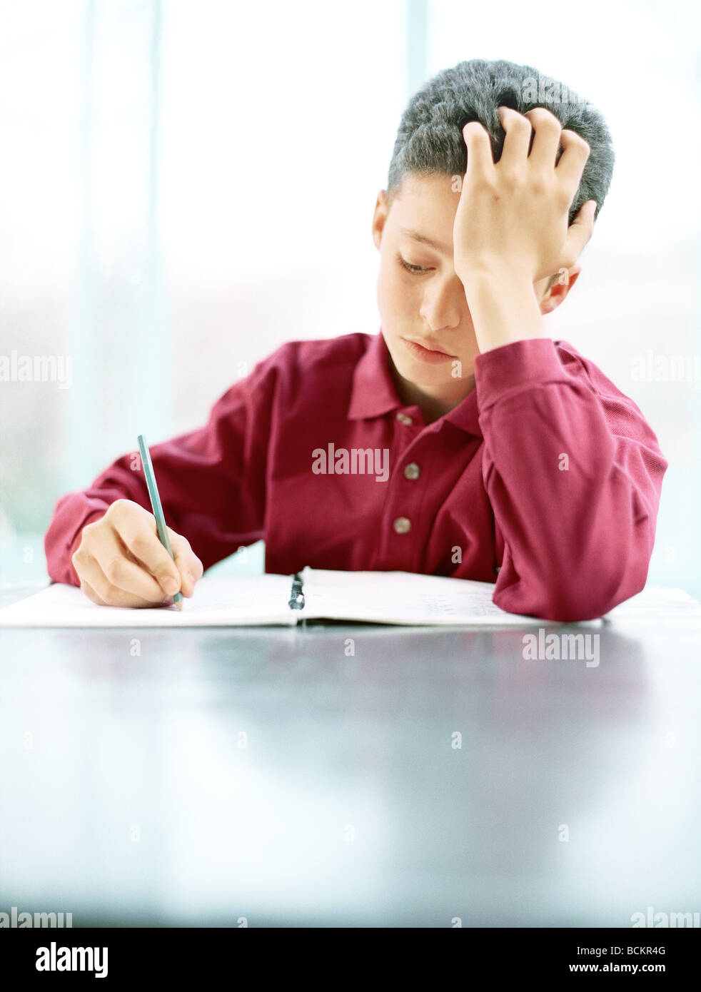 Boy writing at table with hand on forehead, front view Stock Photo - Alamy