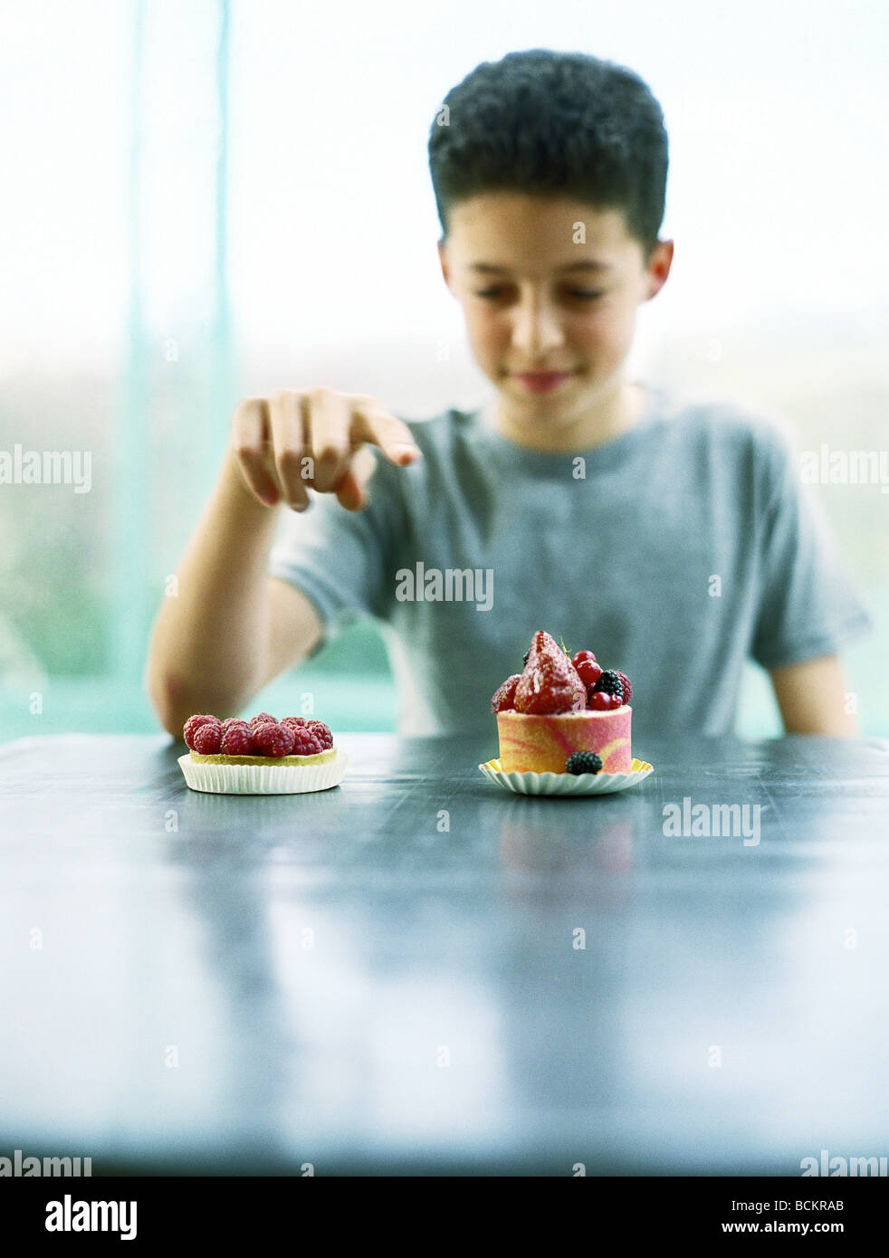 Boy sitting at table, looking at two pastries, pointing Stock Photo - Alamy