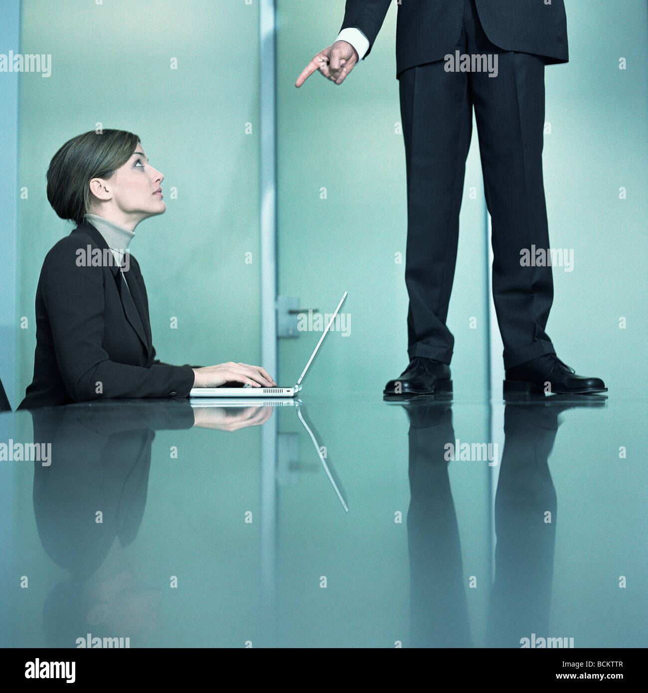 Woman sitting at table working on laptop, man standing on table ...